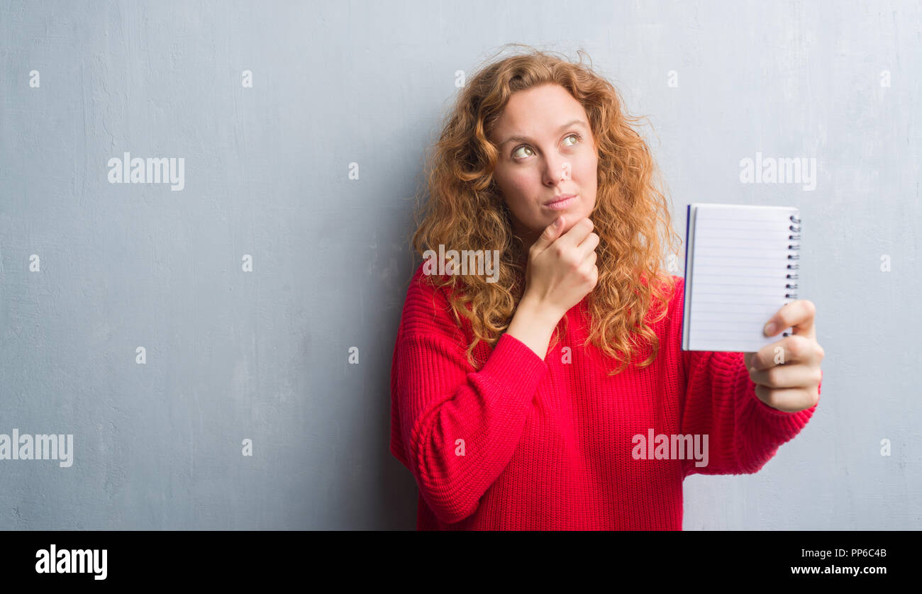 Young redhead woman over grey grunge wall showing blank notebook ...