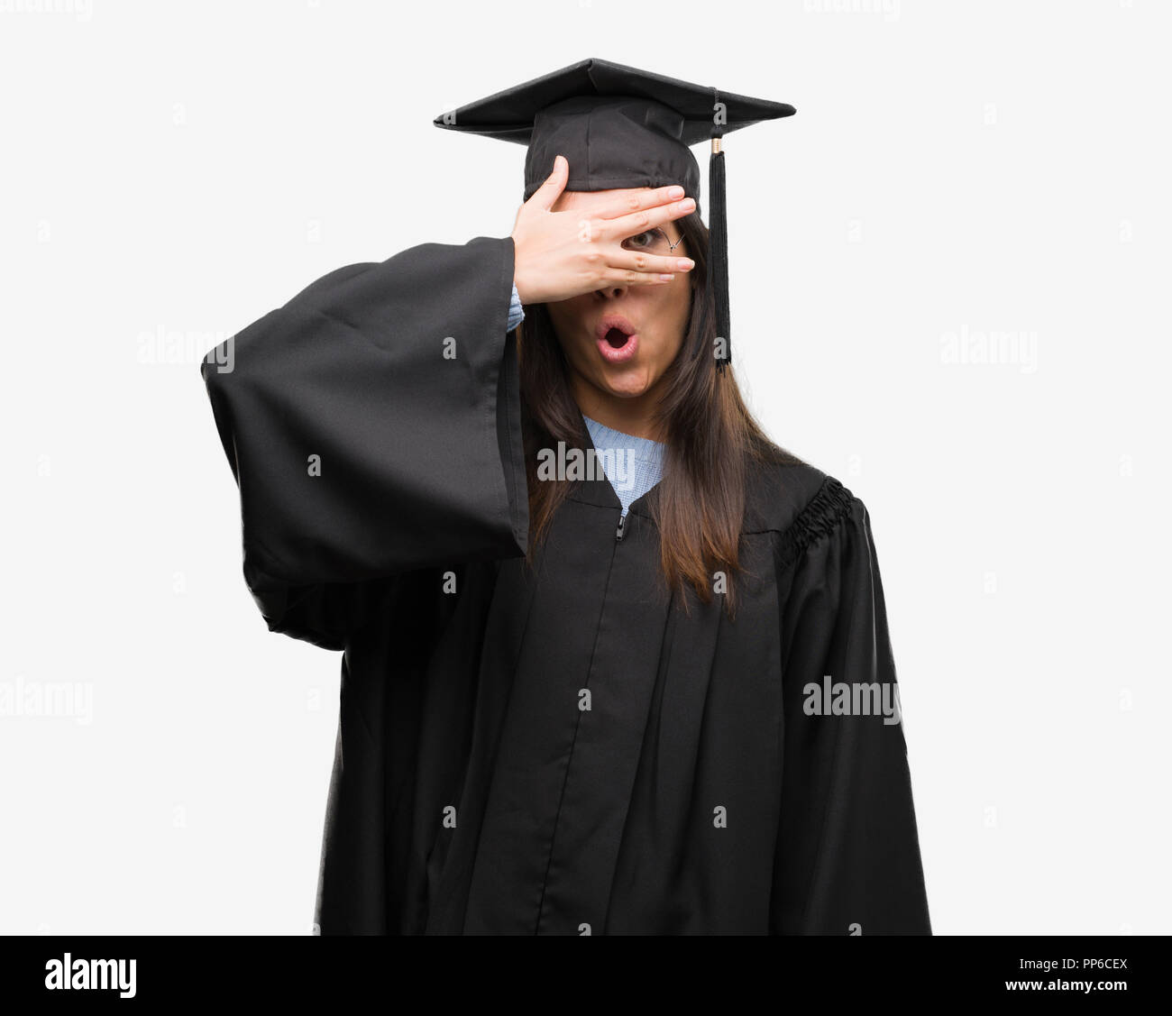 Young hispanic woman wearing graduated cap and uniform peeking in shock ...
