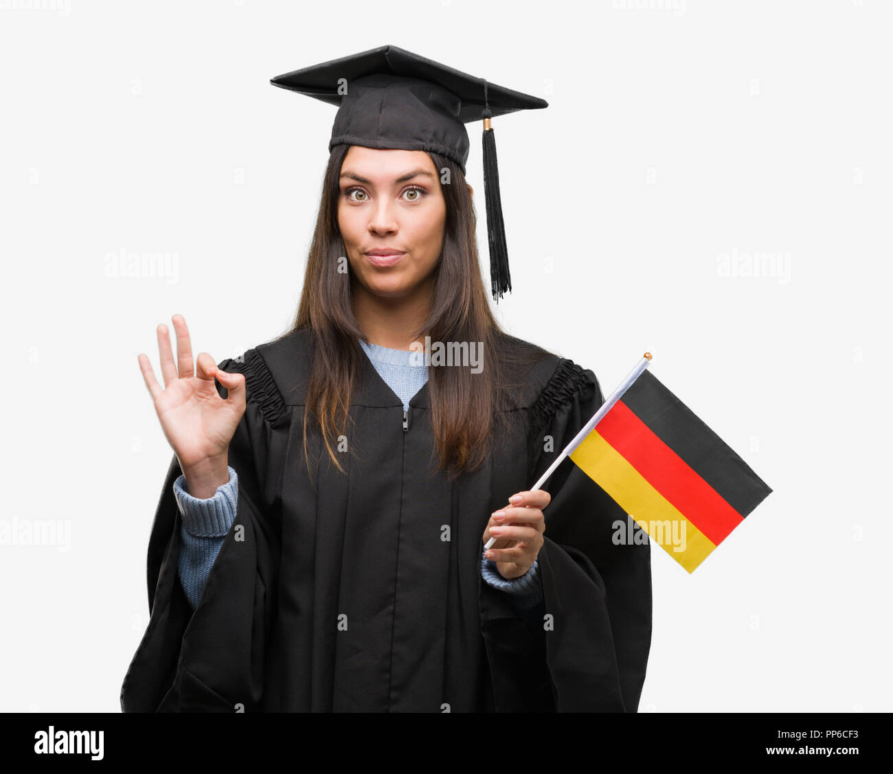 Young hispanic woman wearing graduated uniform holding flag of germany ...
