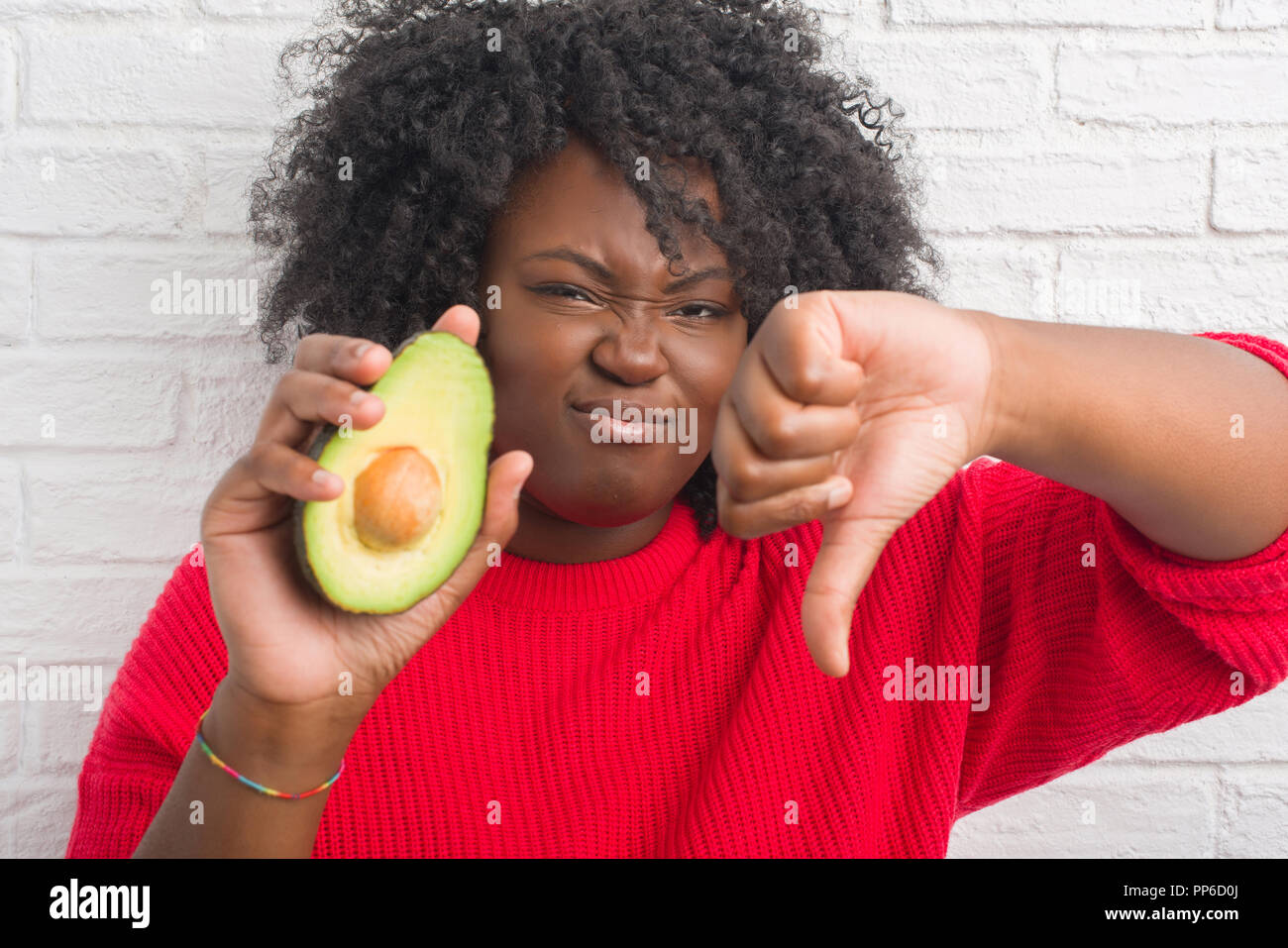 Young african american woman over white brick wall eating avocado with ...