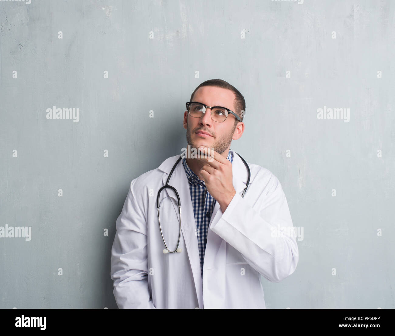 Young caucasian man over grey grunge wall wearing doctor uniform ...