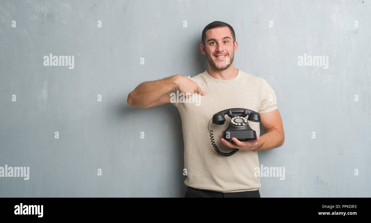 Young caucasian man over grey grunge wall calling using vintage ...