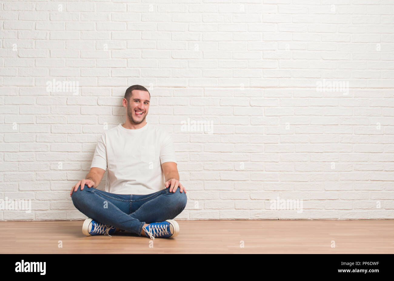 Young caucasian man sitting on the floor over white brick wall sticking ...