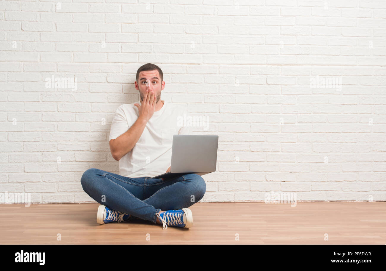 Young caucasian man sitting over white brick wall using computer laptop ...