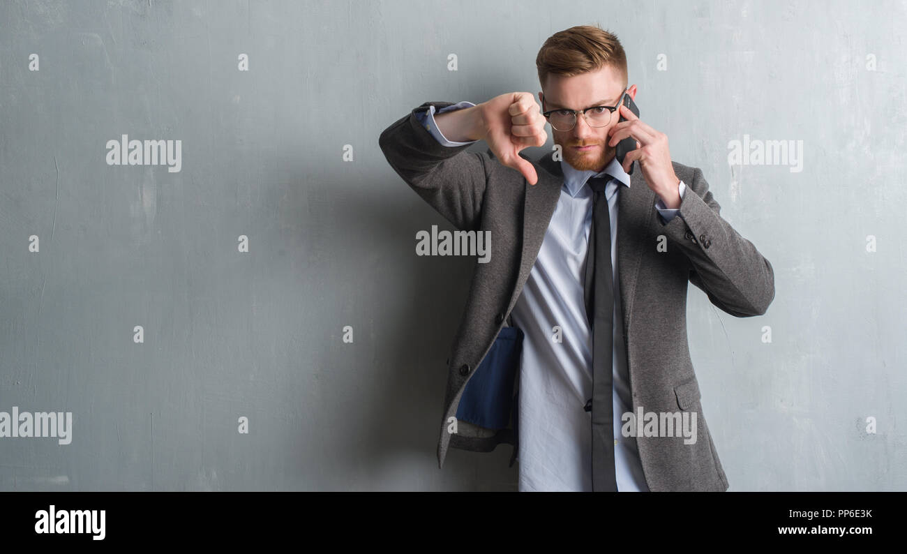 Young redhead business man over grey grunge wall talking on the phone ...