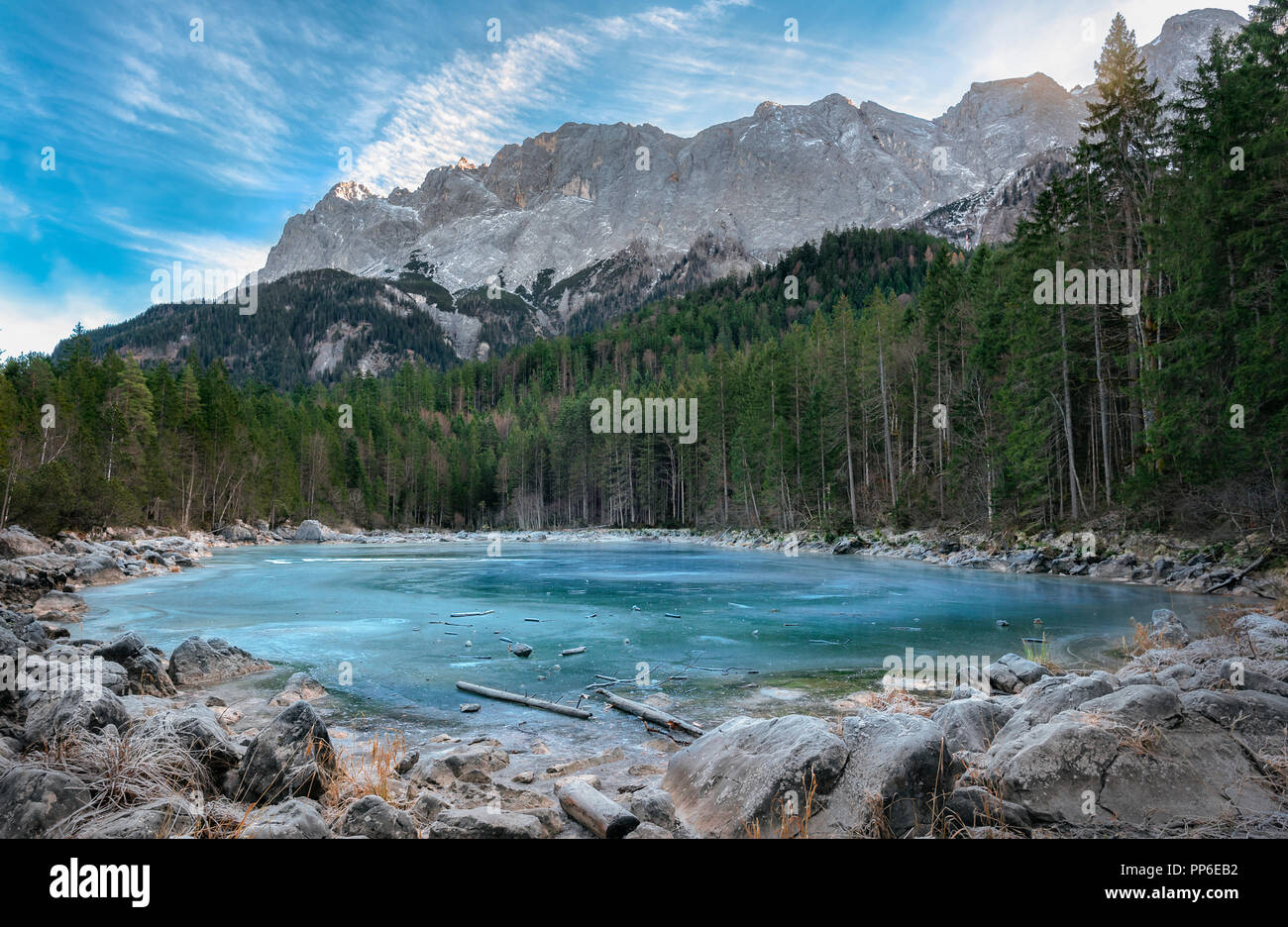 Alpine lake with blue frozen water, surrounded by fir forest and the ...