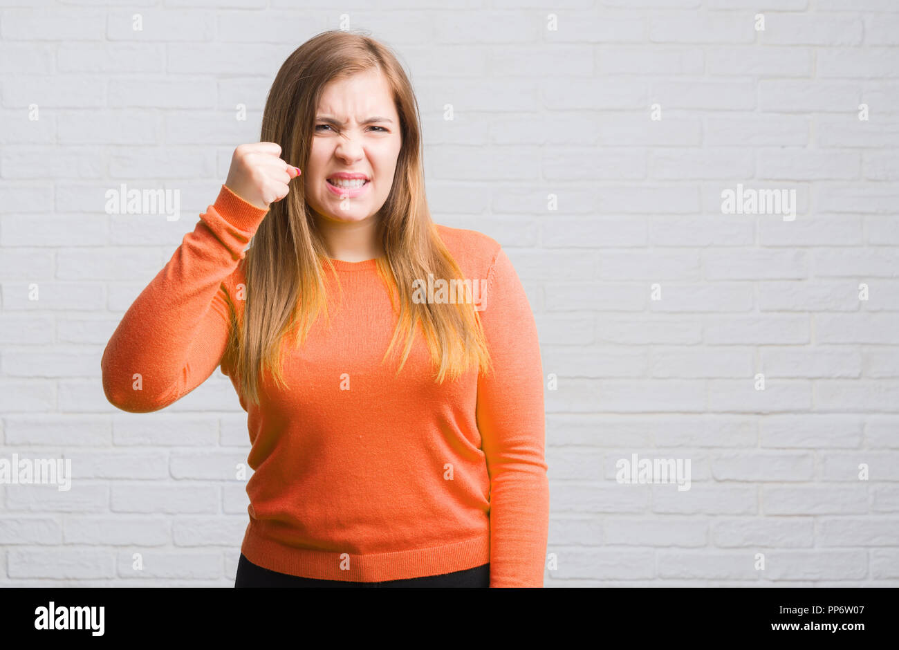 Young adult woman over white brick wall annoyed and frustrated shouting ...