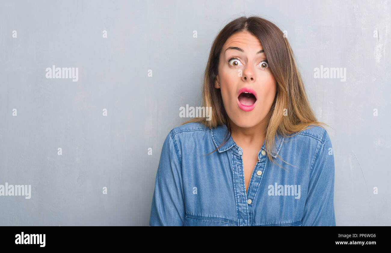 Young adult woman over grunge grey wall wearing denim outfit afraid and ...