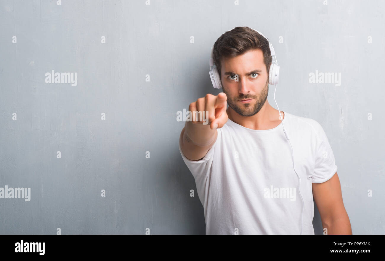 Handsome young man over grey grunge wall wearing headphones listening ...
