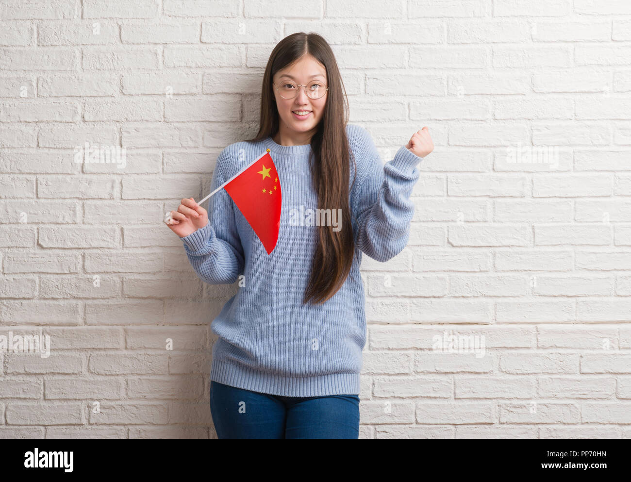Young Chinese woman over brick wall holding flag of China screaming ...
