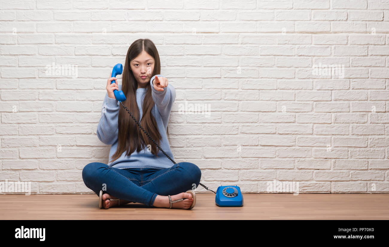 Young Chinese woman calling using vintage telephone pointing with ...
