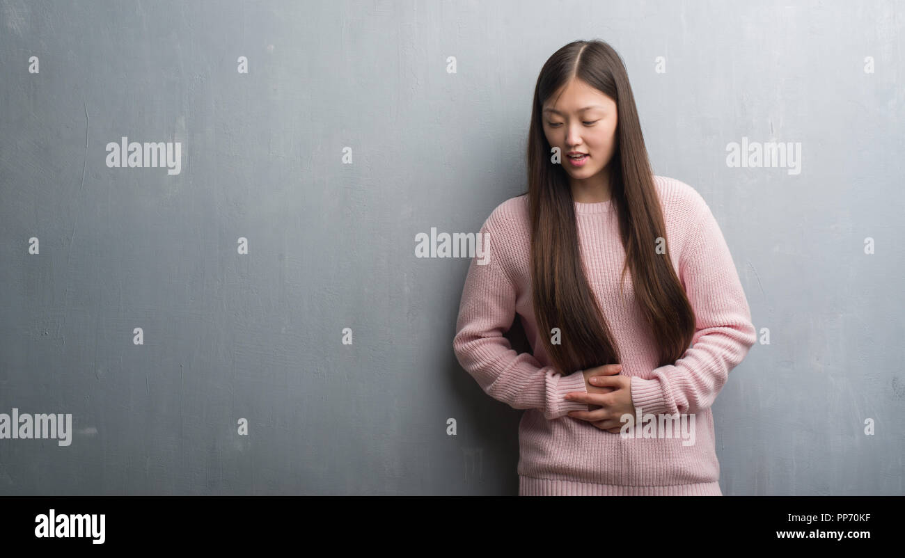 Young Chinese woman over grey wall with hand on stomach because ...