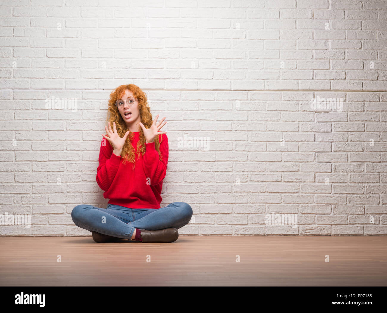 Young redhead woman sitting over brick wall afraid and terrified with ...