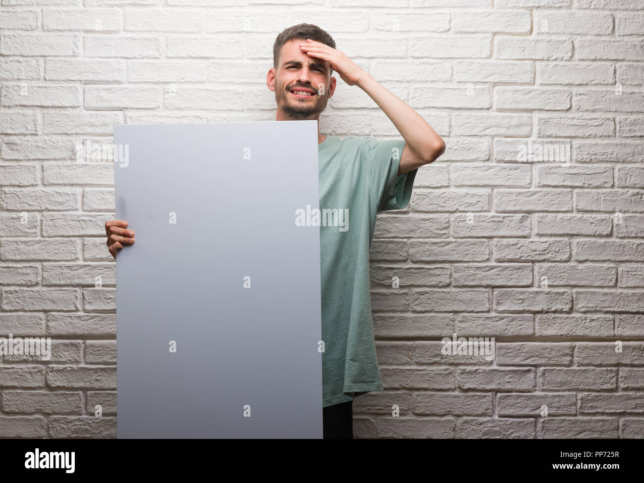 Young adult man over brick wall holding banner stressed with hand on ...