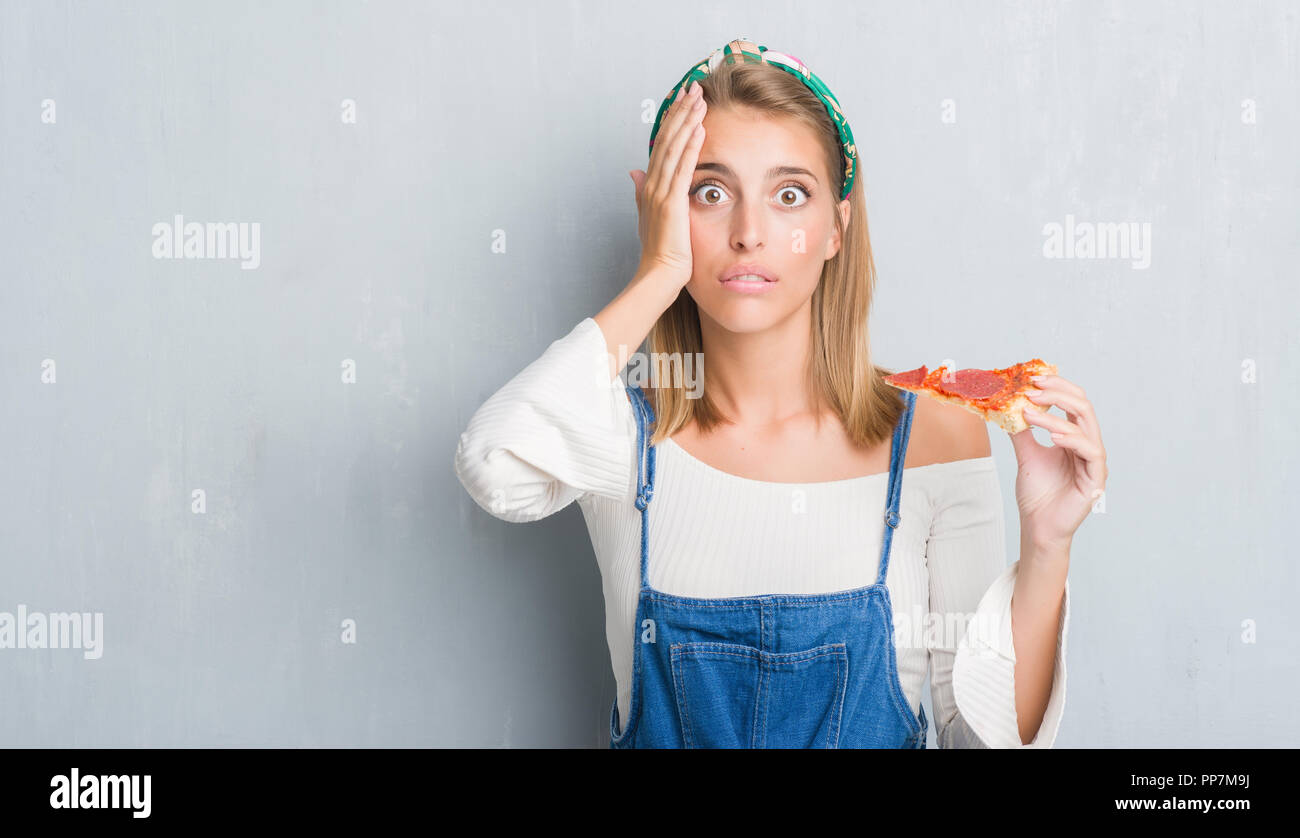 Beautiful young woman over grunge grey wall eating pepperoni pizza ...