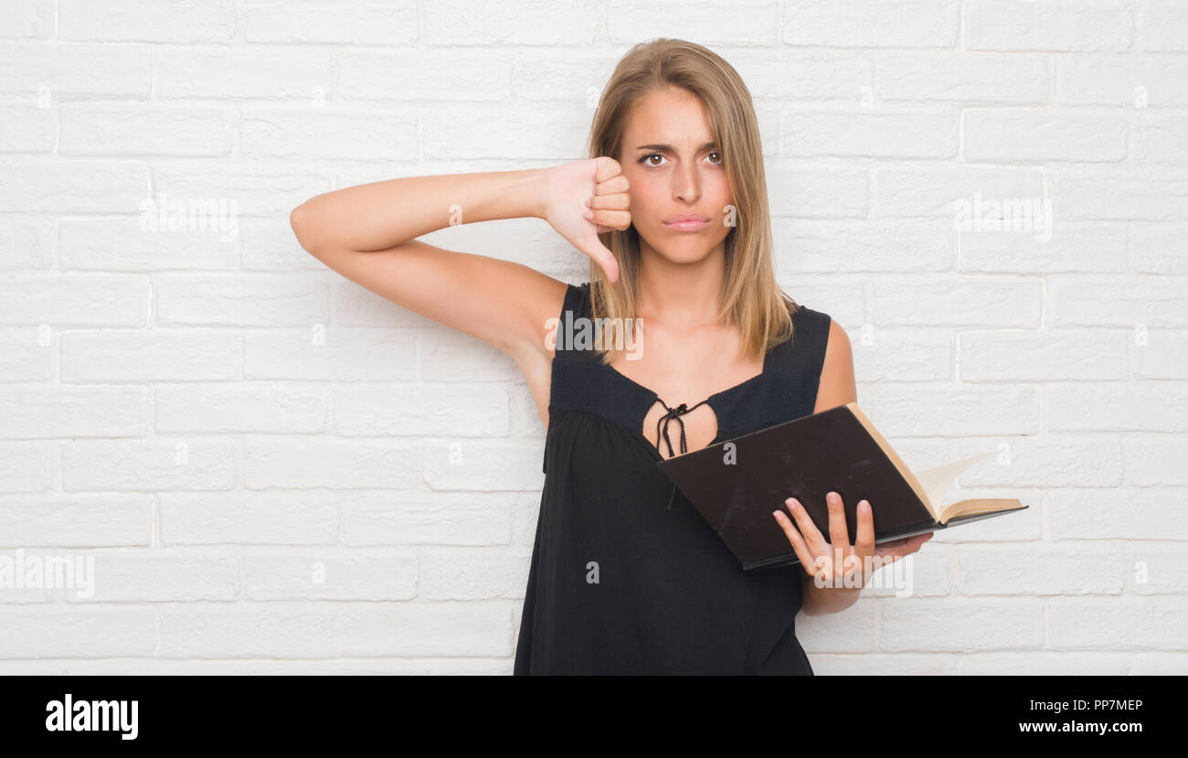 Beautiful young woman over white brick wall reading a book with angry ...