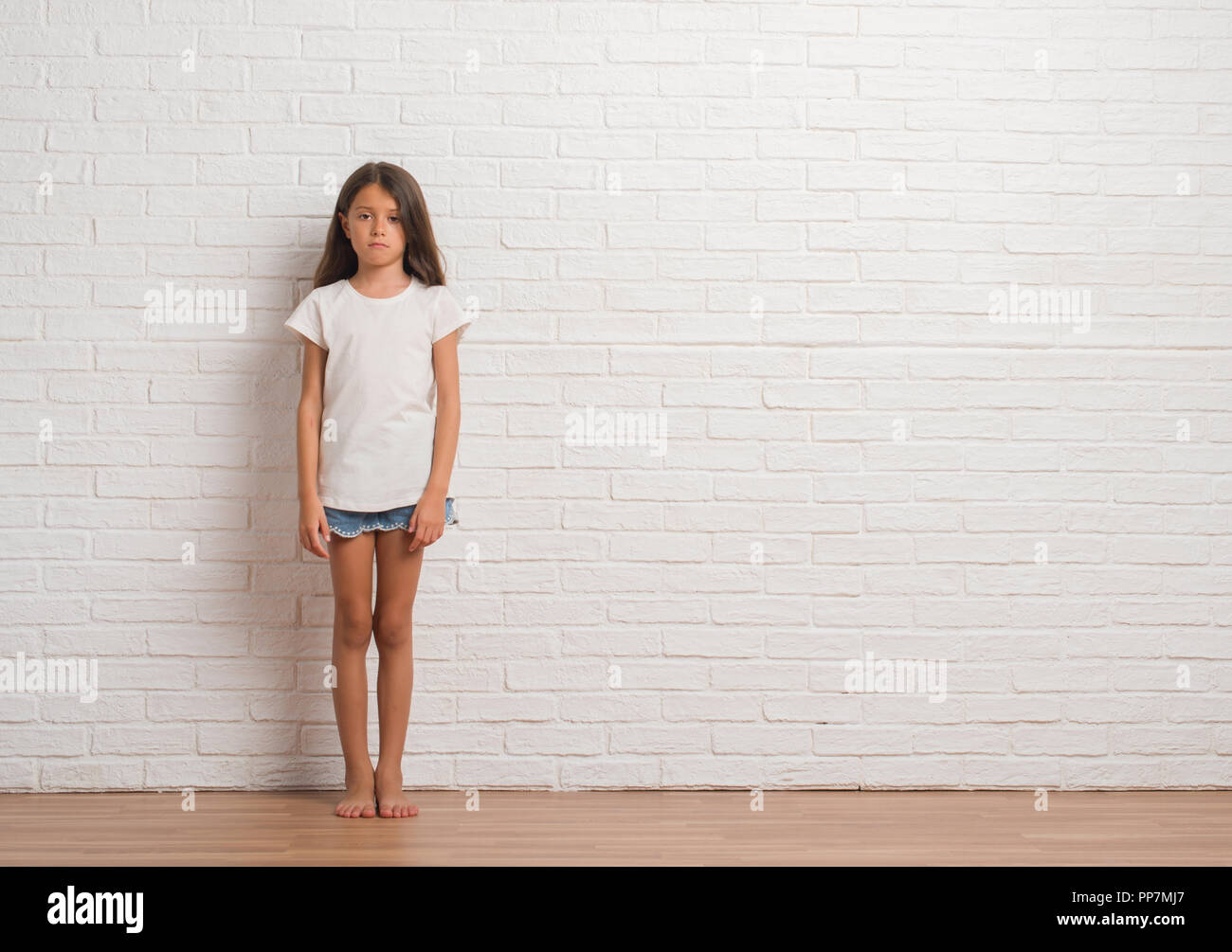Young hispanic kid stading over white brick wall depressed and worry ...