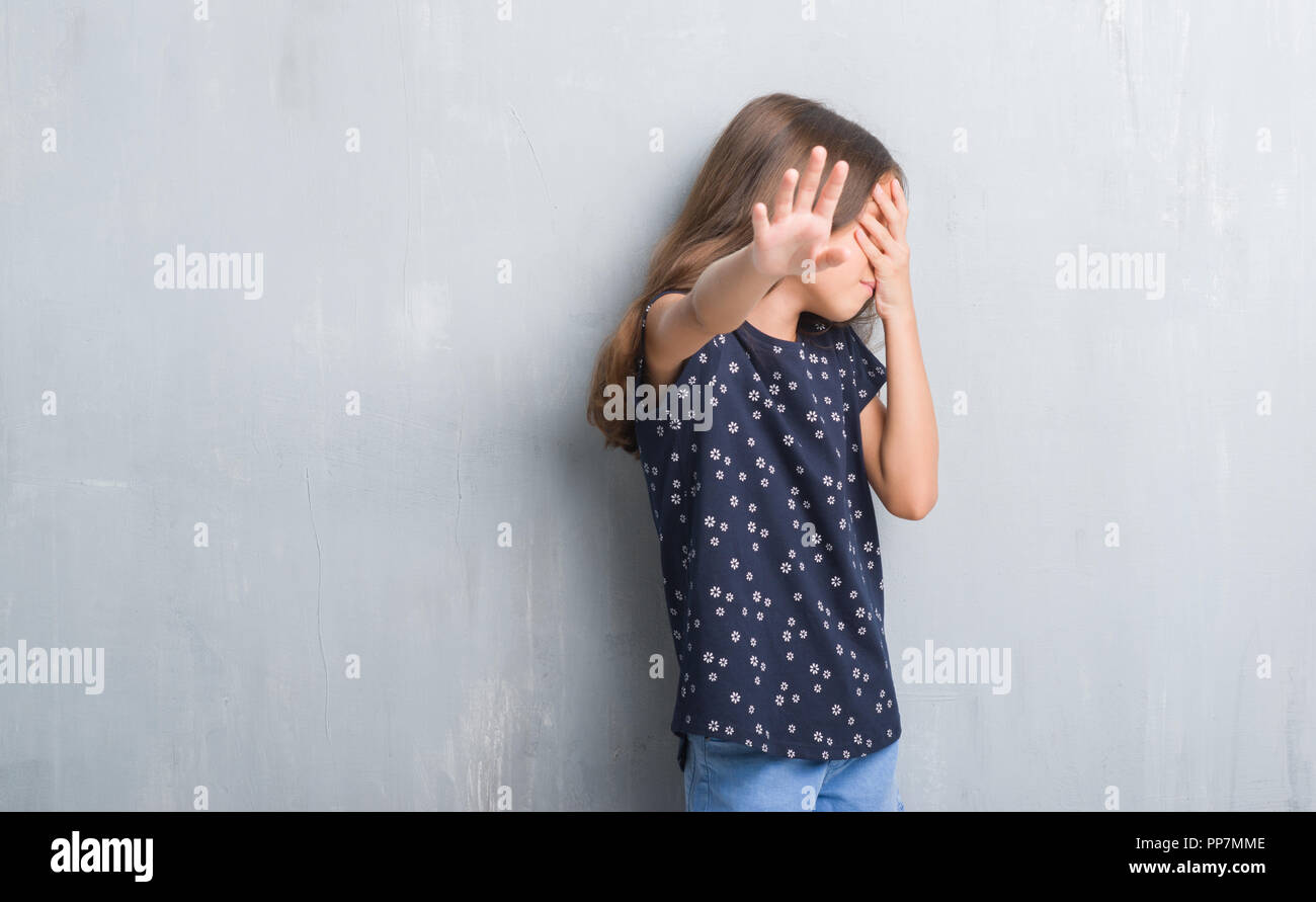 Young hispanic kid over grunge grey wall covering eyes with hands and ...