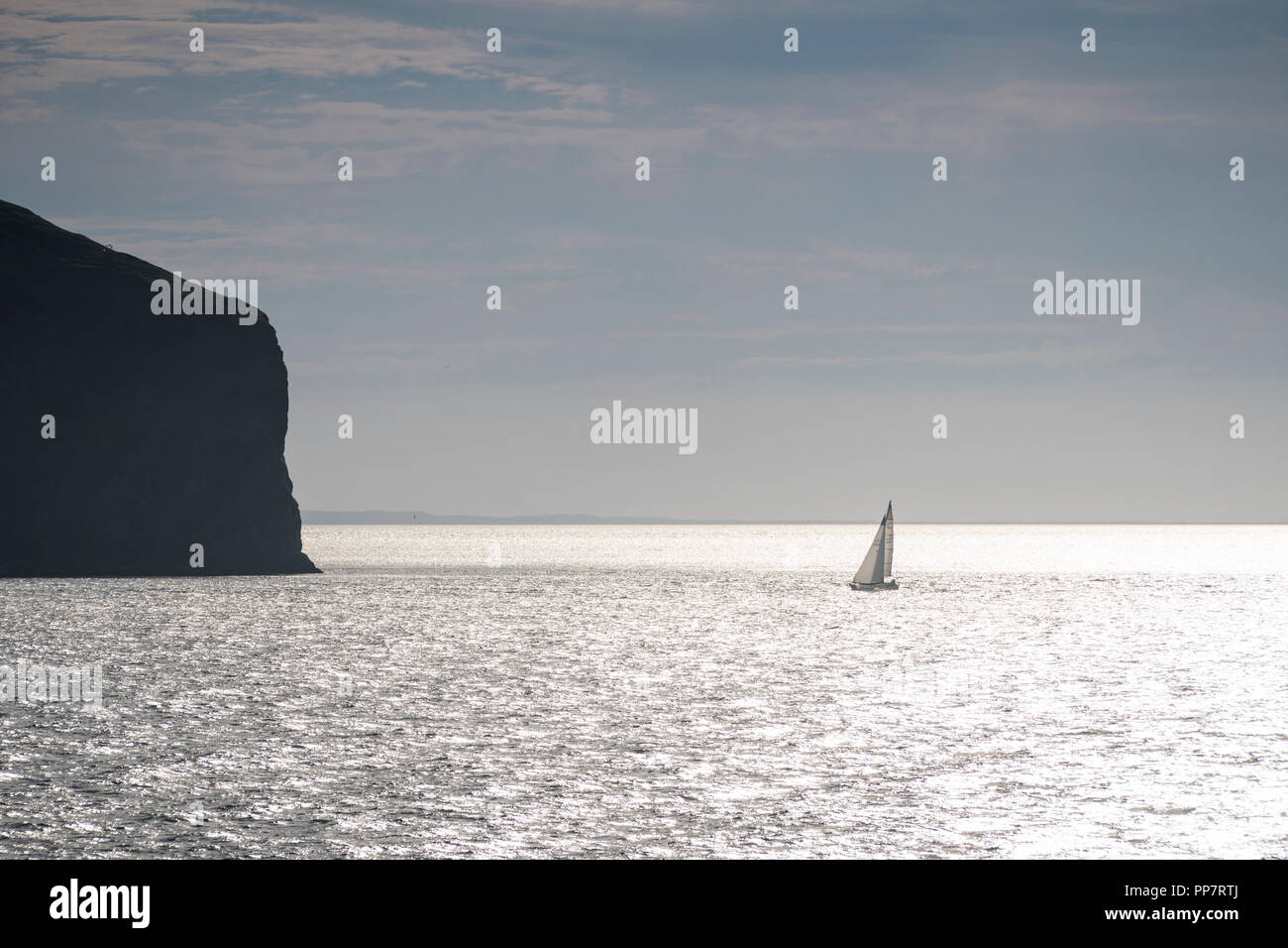 Sailboat on sun-reflecting water heading past Entry Island in the ...