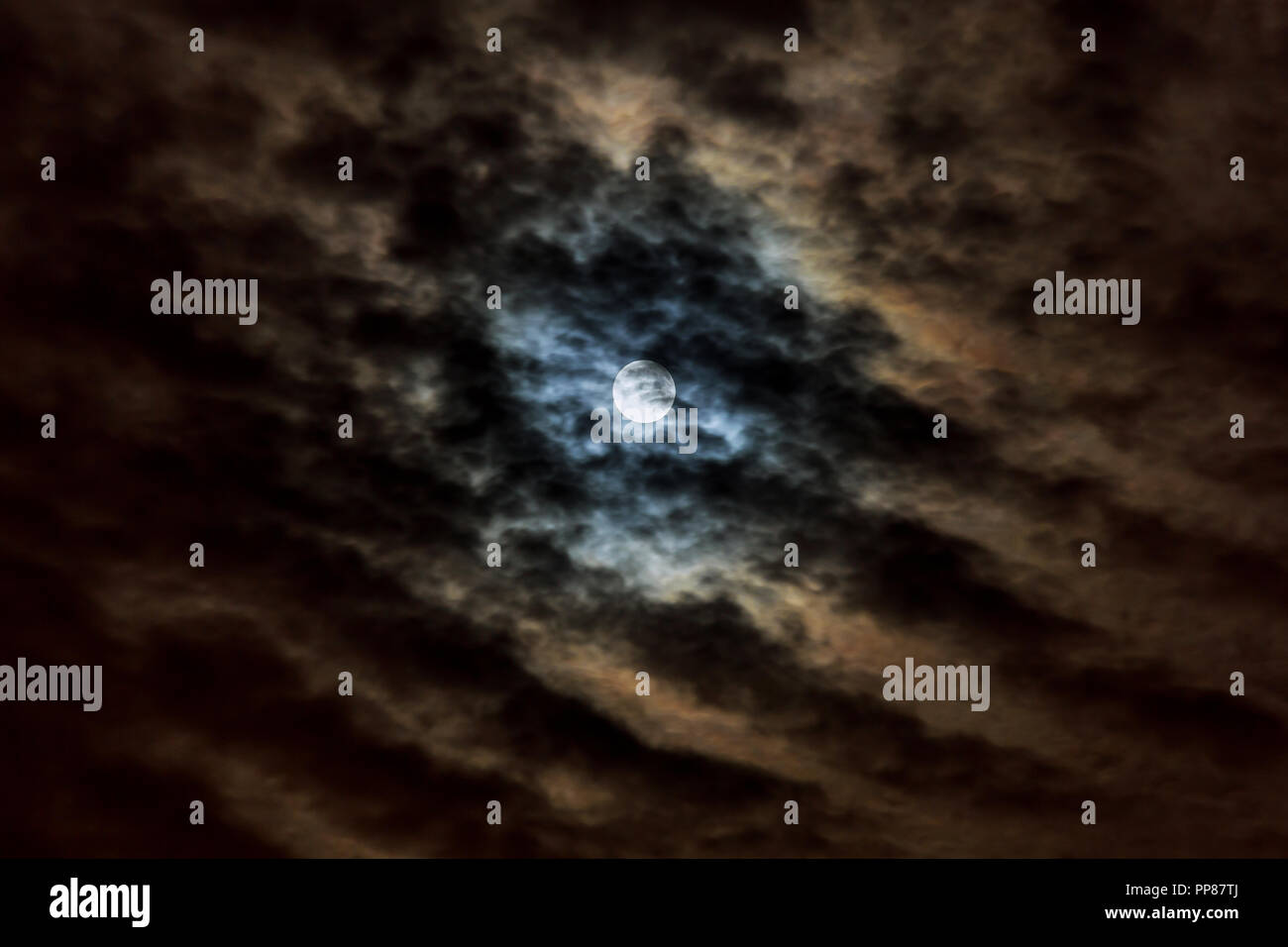 Full moon rises behind strong clouds in a clear night and eerie white ...