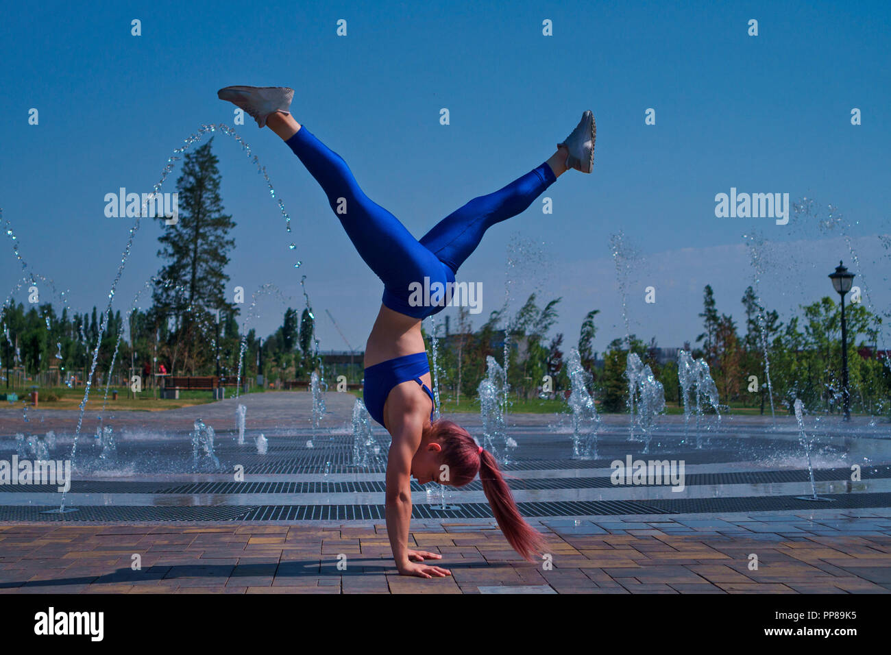 Girl on street workout. Slender young woman makes stand on her hands ...