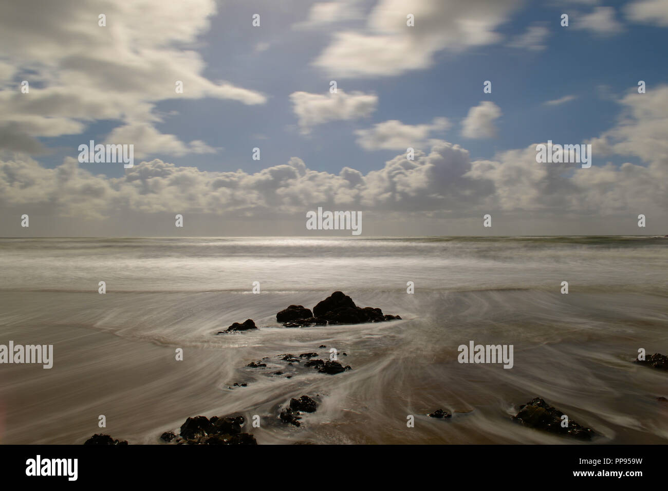 Receding waves leave a swirling pattern around a rock with dramatic sky ...