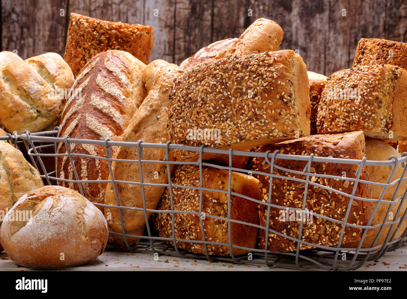 Different types of bread and buns in a metal basket on a wooden ...