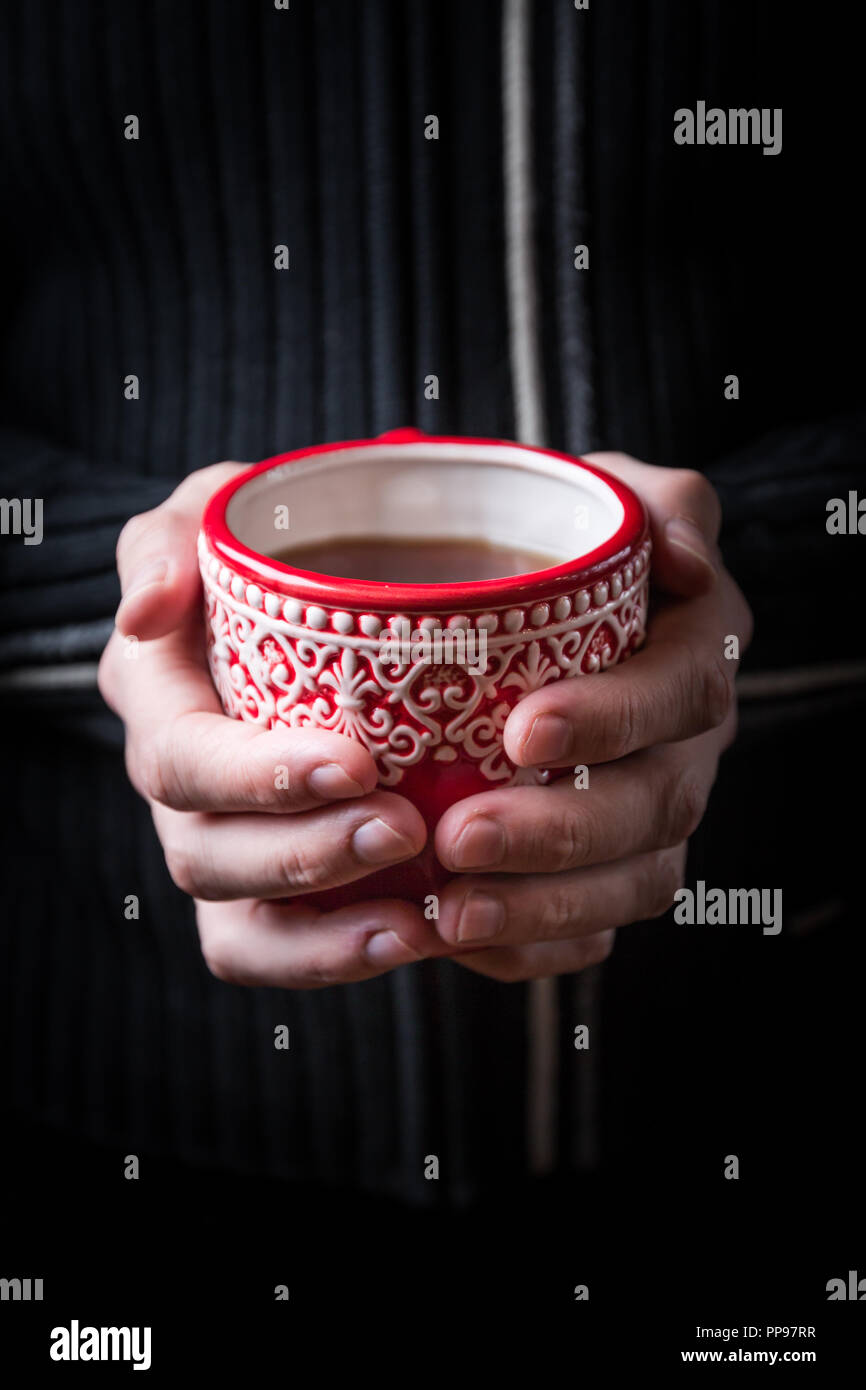 Close up of male hands holding red mug with hot drink on black ...