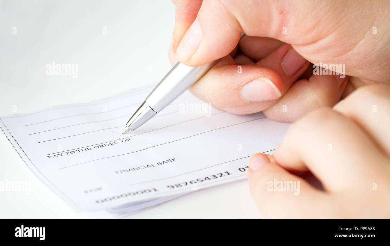 Closeup image of hand filling personal bank cheque with pen Stock Photo ...