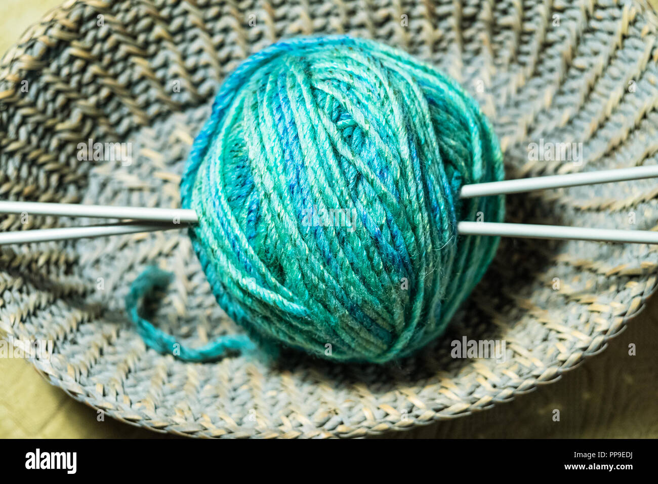 ball of two-tone yarn with knitting needles on a straw plate Stock ...