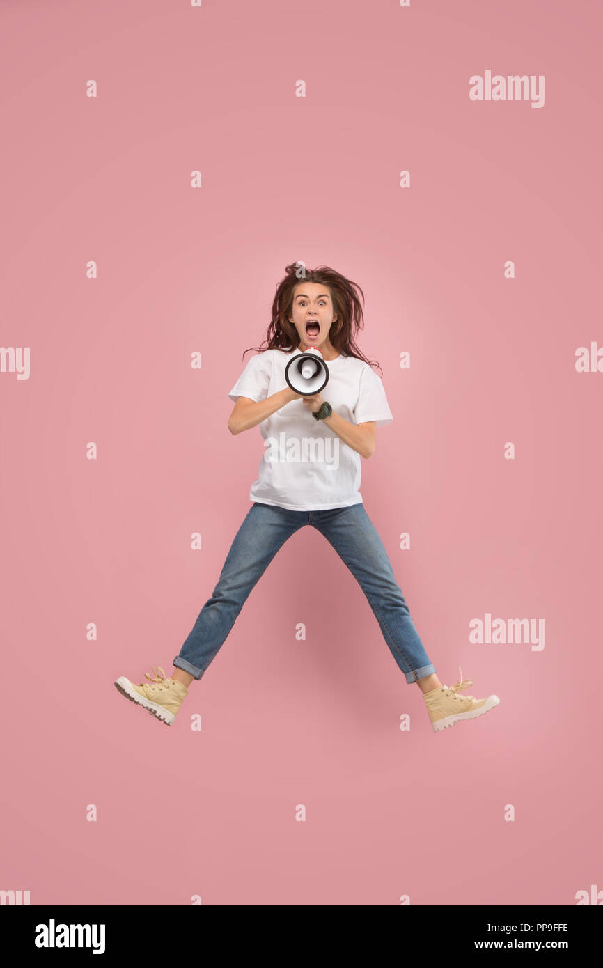 Beautiful young woman jumping with megaphone isolated over pink ...