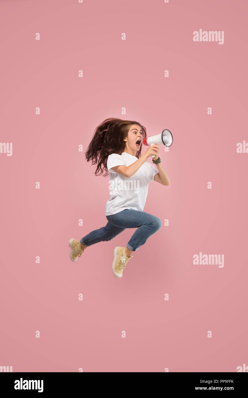 Beautiful young woman jumping with megaphone isolated over pink ...