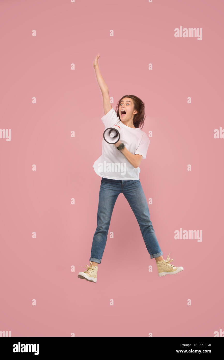 Beautiful young woman jumping with megaphone isolated over pink ...