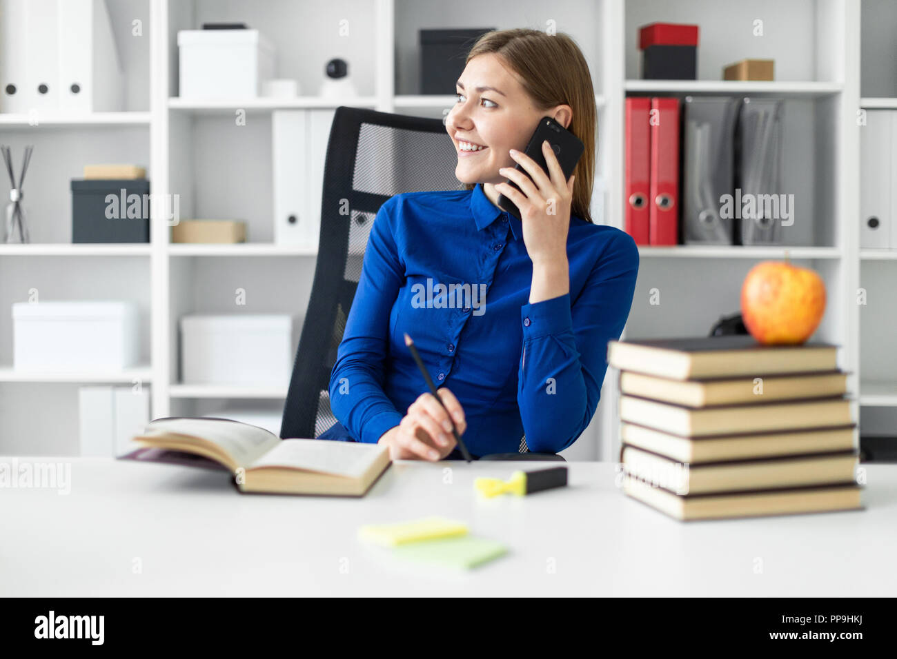 A young girl is sitting at a computer desk, holding a pencil in her ...