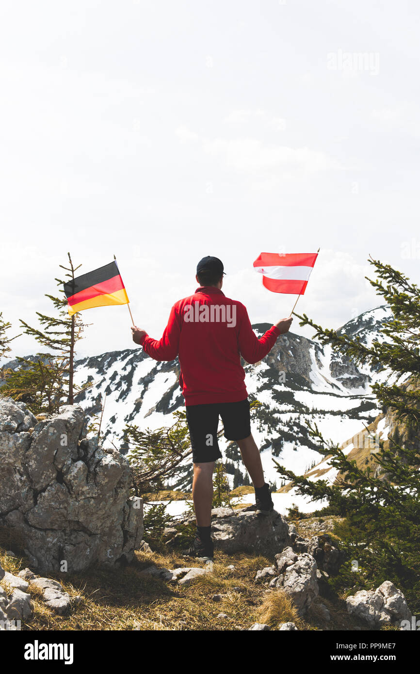 male hiker with red sweater is holding a german and an austrian flag in ...