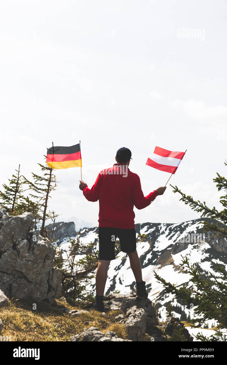 male hiker with red sweater is holding a german and an austrian flag in ...