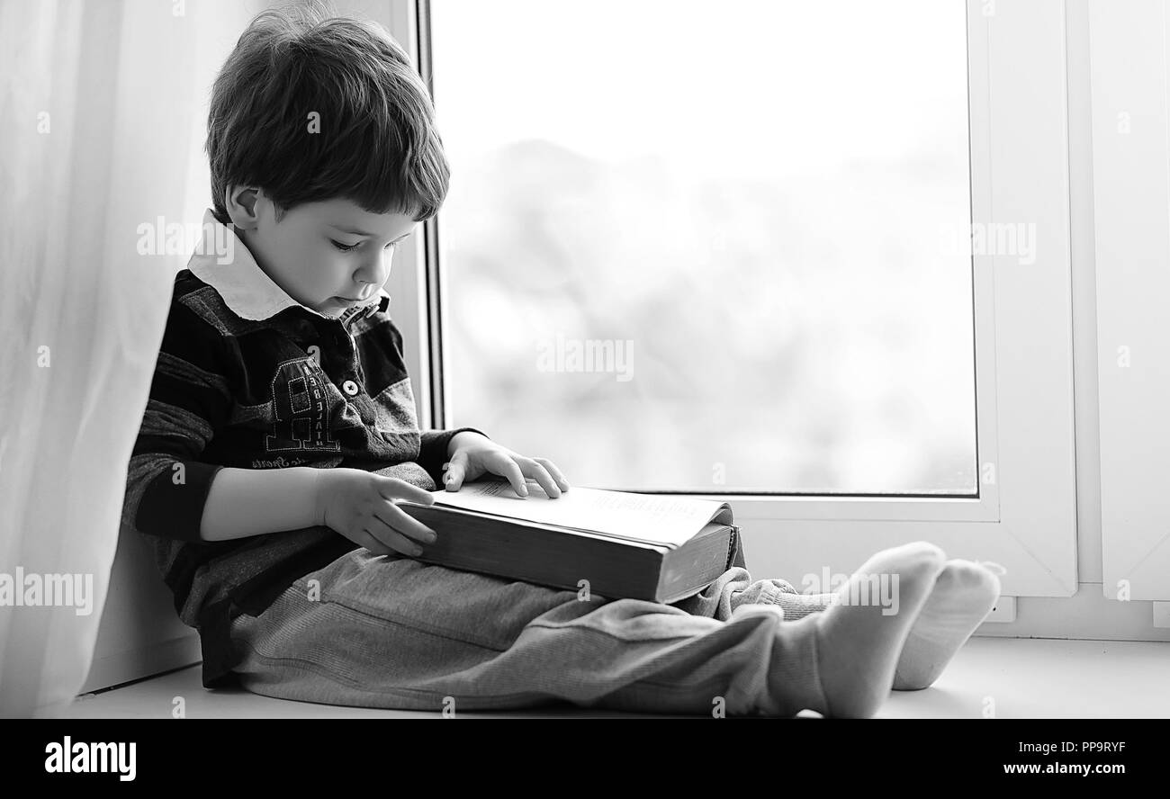 The little boy is reading a book. The child sits at the window a Stock ...