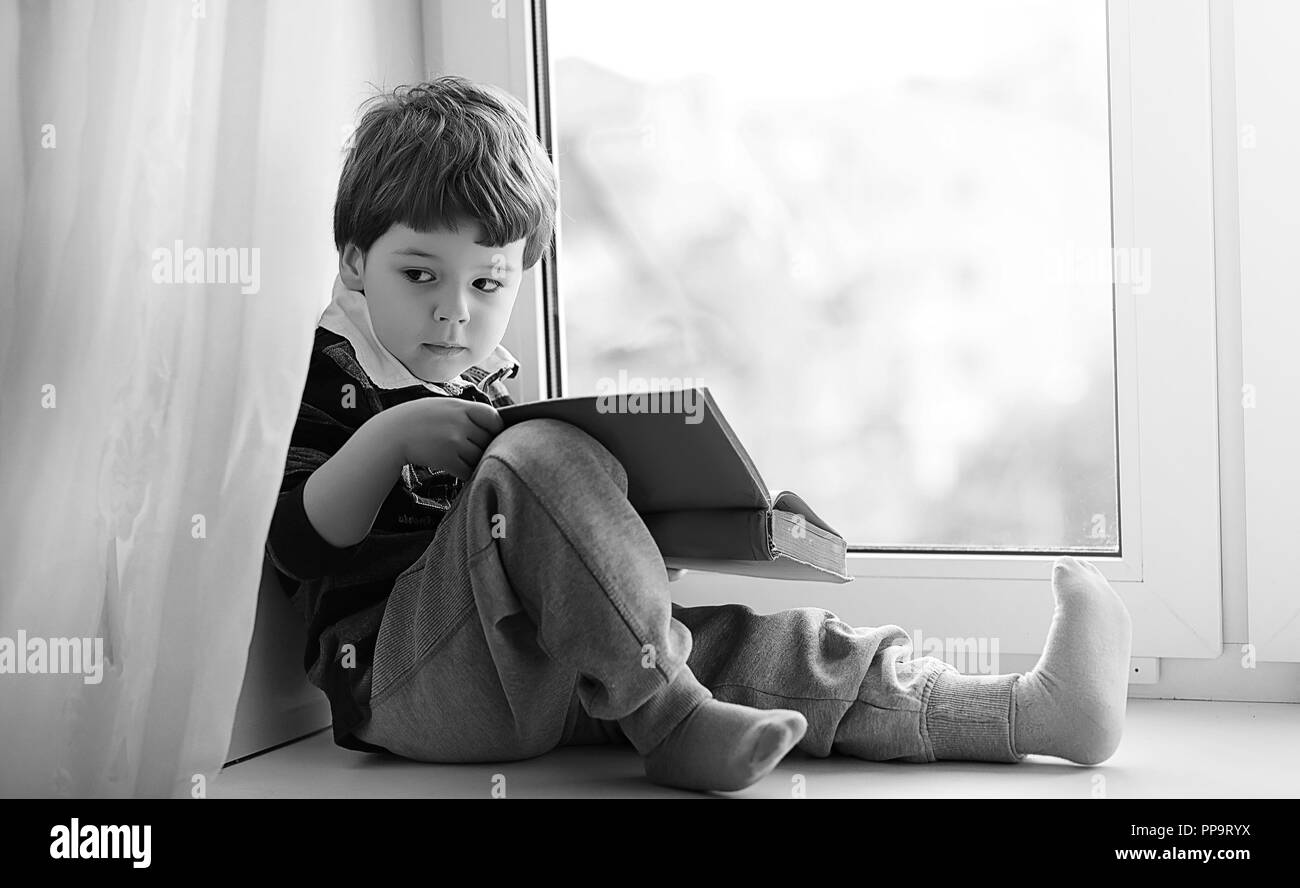 The little boy is reading a book. The child sits at the window a Stock ...
