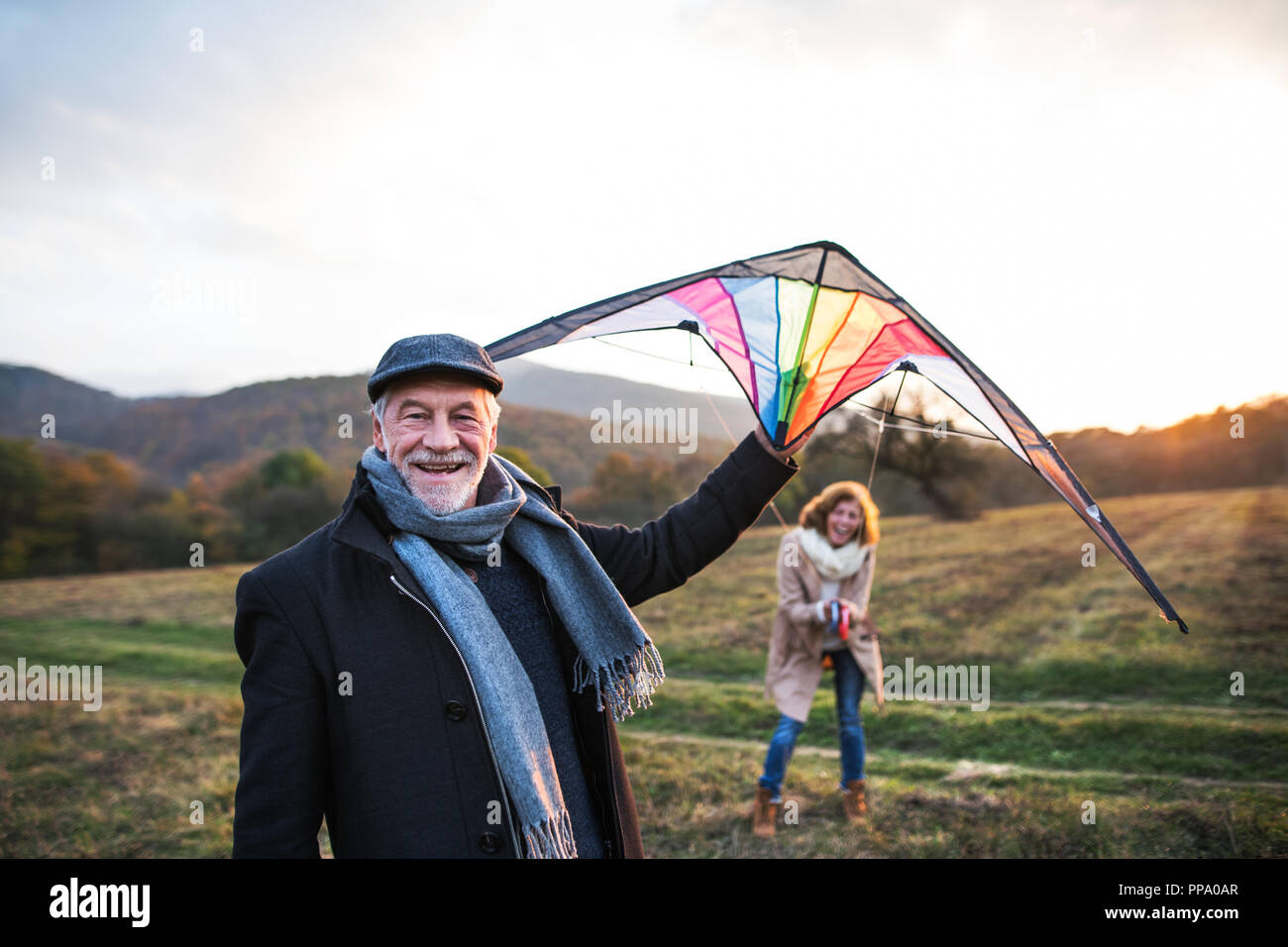 Carefree senior couple flying a kite in an autumn nature at sunset ...