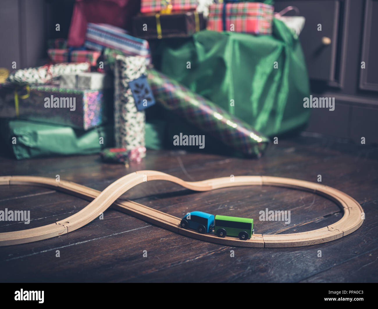 A wooden toy train and track setup on the floor with a christmas tree ...