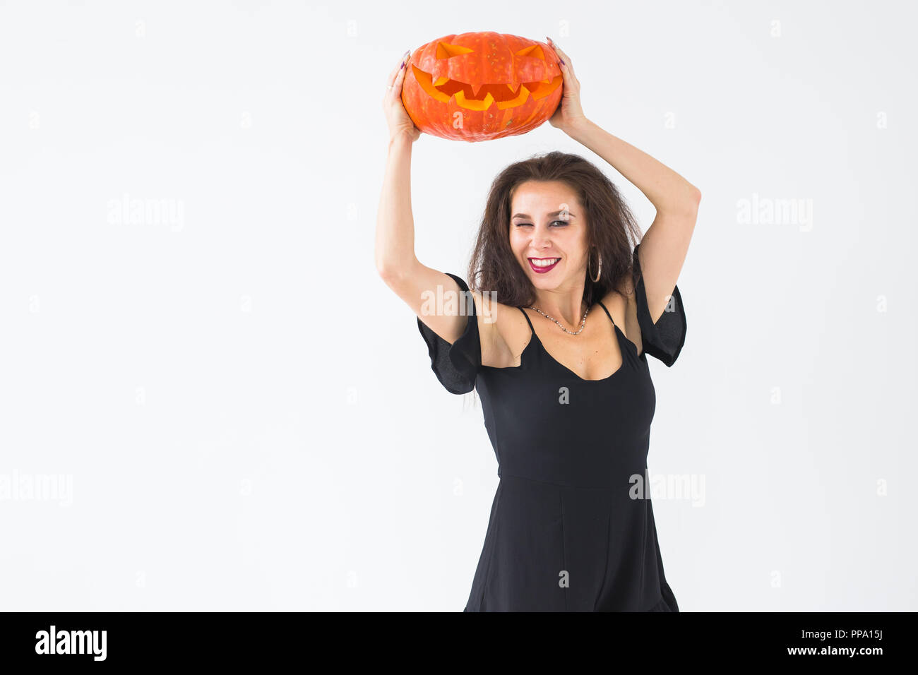 Smiling brunette woman in halloween makeup posing with carved pumpkin ...