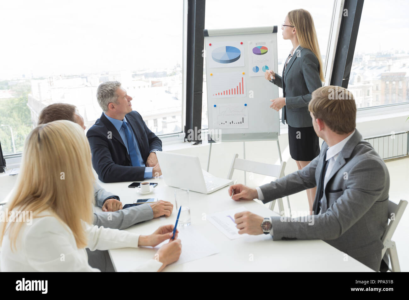 Businesswoman giving a presentation to her colleagues at work standing ...
