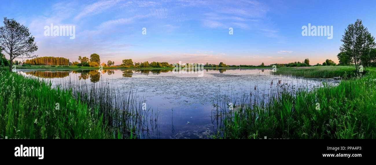 countryside scene by the lake at sunset with trees over the pond and ...
