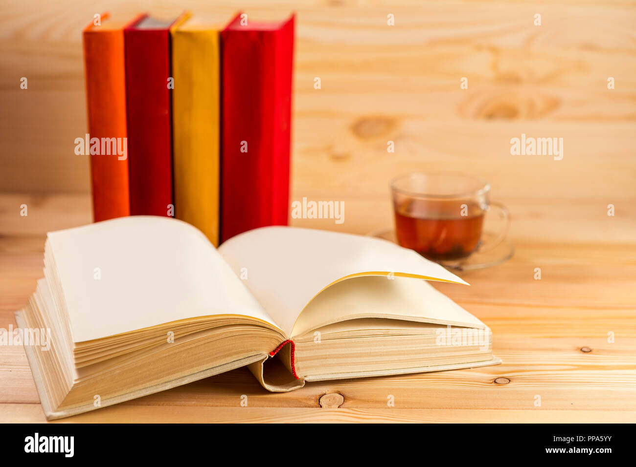 Open book and glass cup of tea and a stack of books with colorful ...