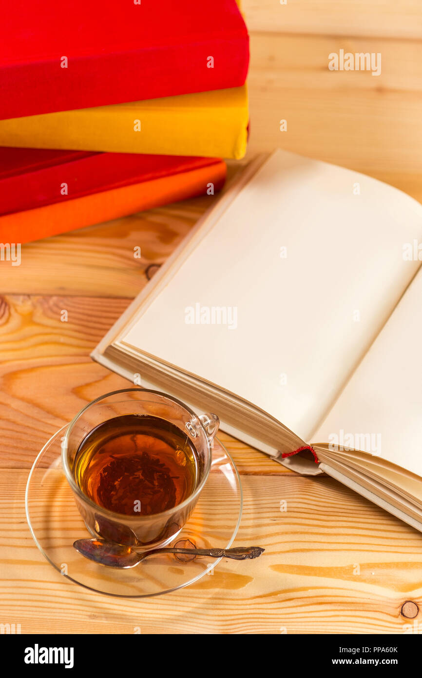 Open book and glass cup of tea and a stack of books with colorful ...
