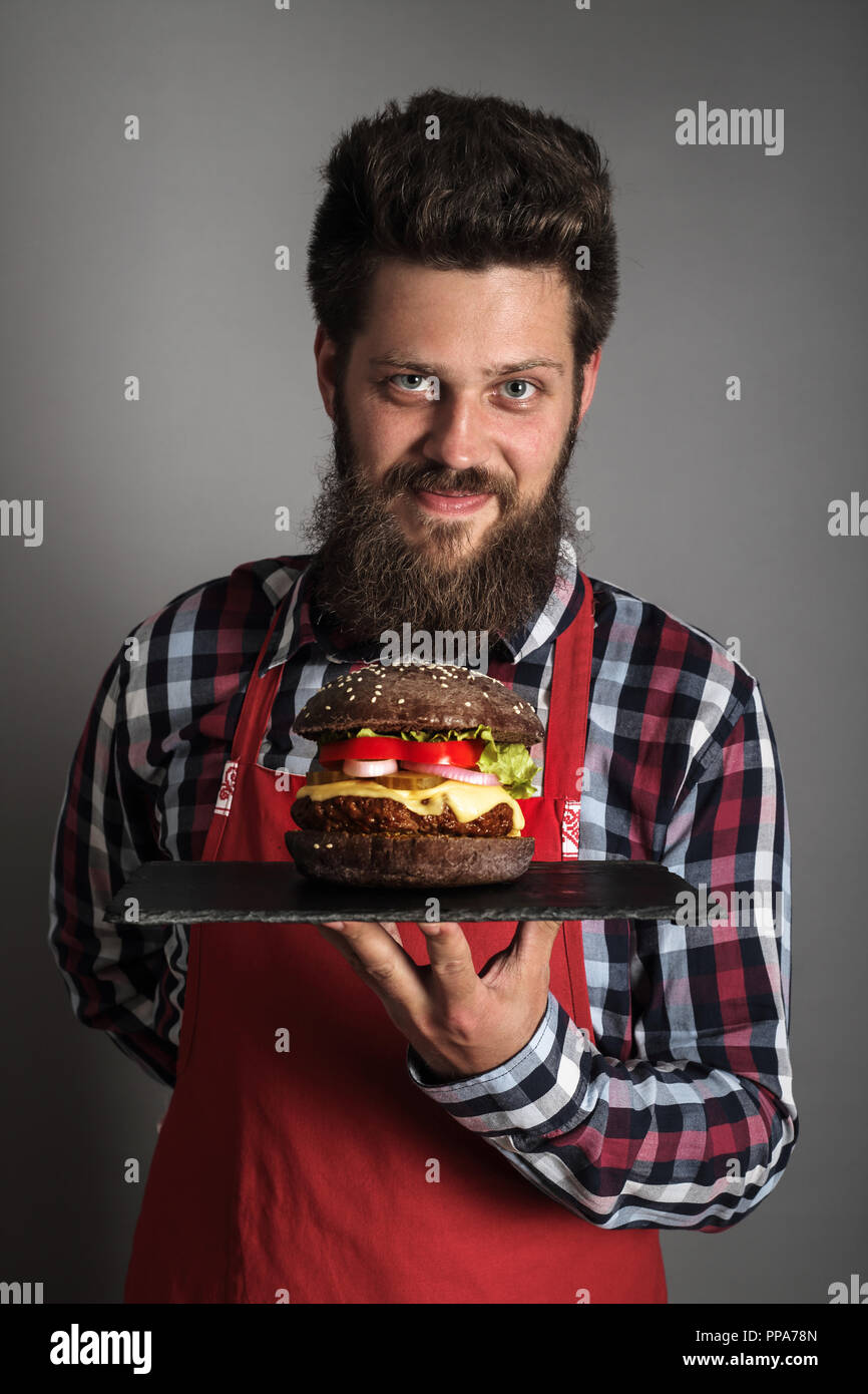 Male cook in red apron giving you fresh self made black burger and ...