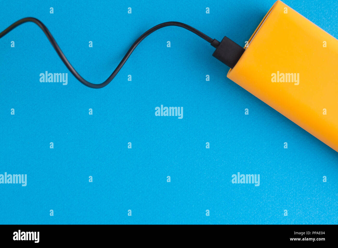 Orange power bank plugged in with black USB cable on an blue background ...