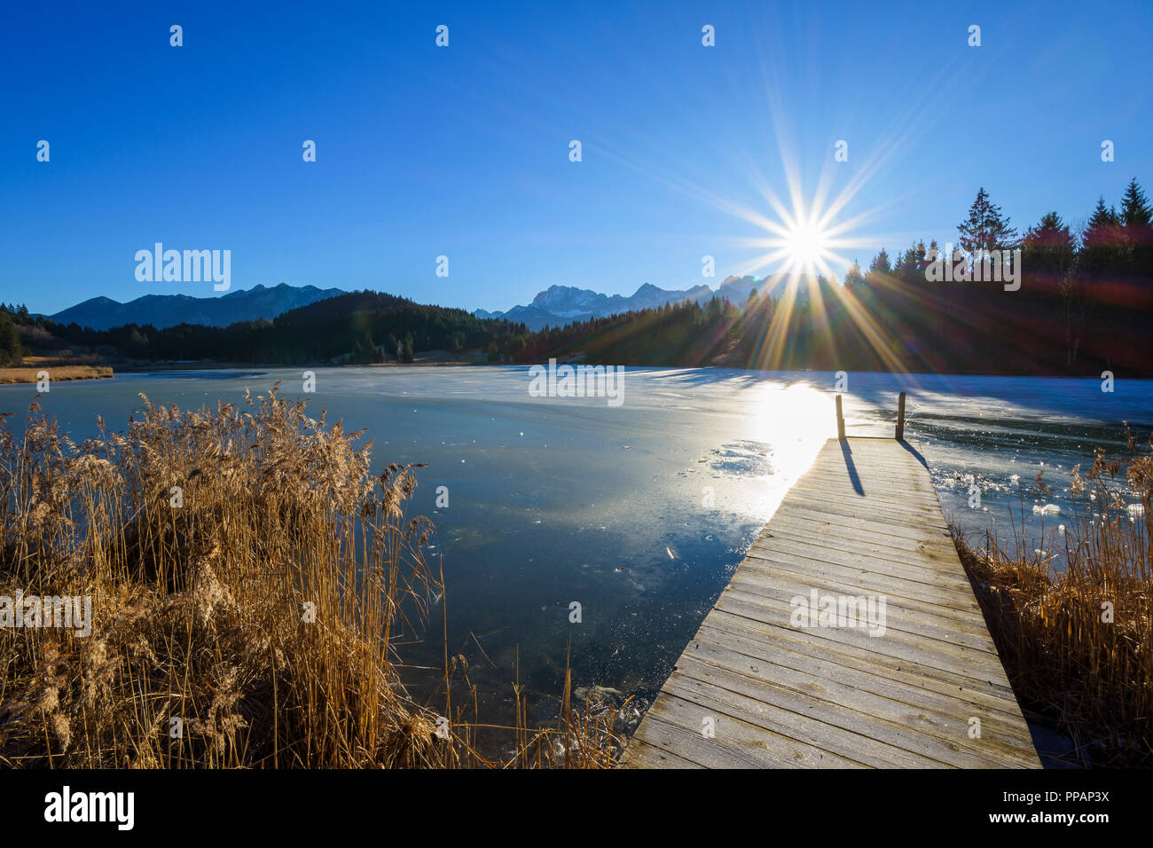 Wooden jetty with frozen lake and sun, Lake Geroldsee, Wagenbruechsee ...