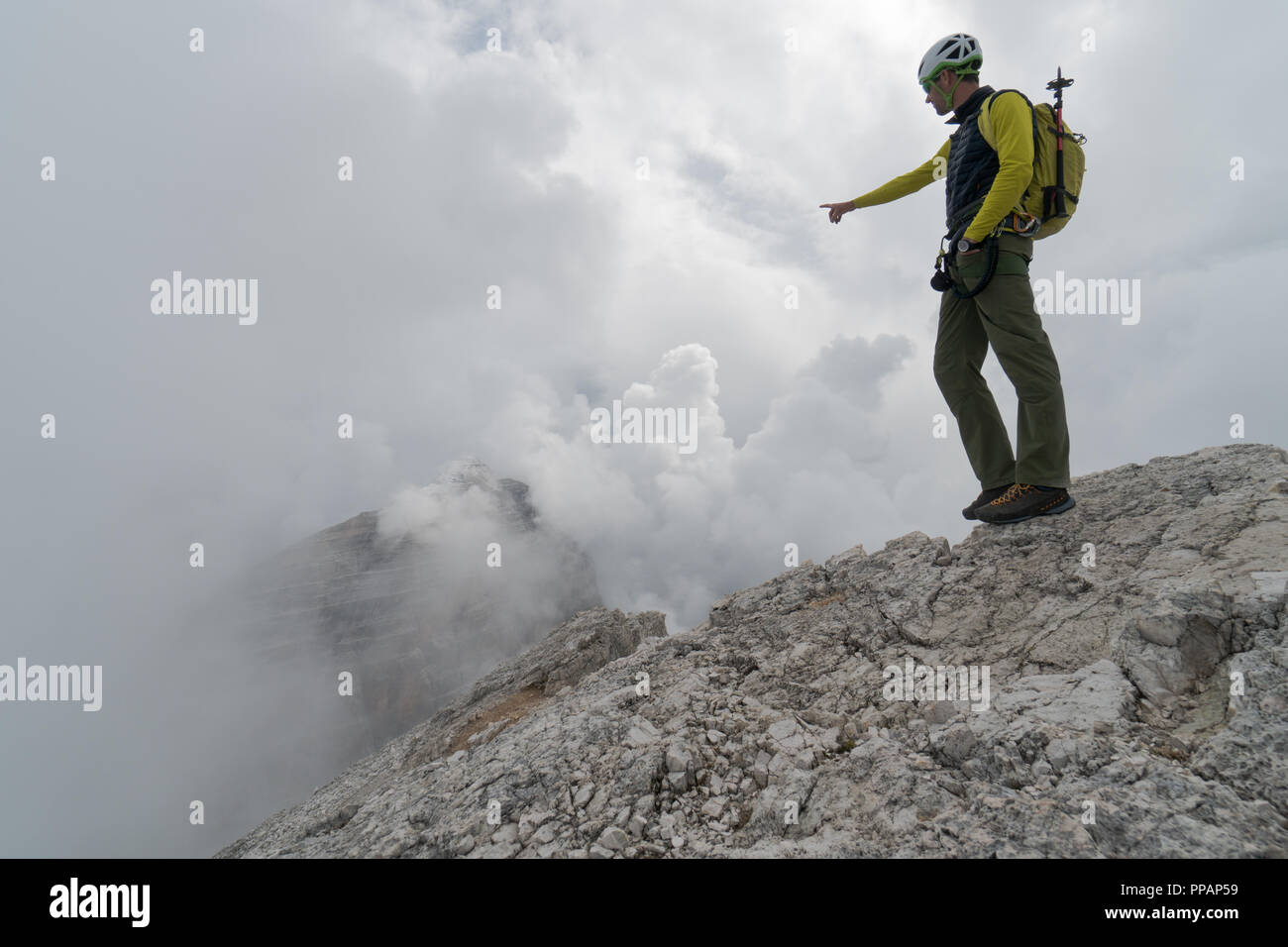 young male mountain guide on a Dolomite mountain peak pointing to the ...