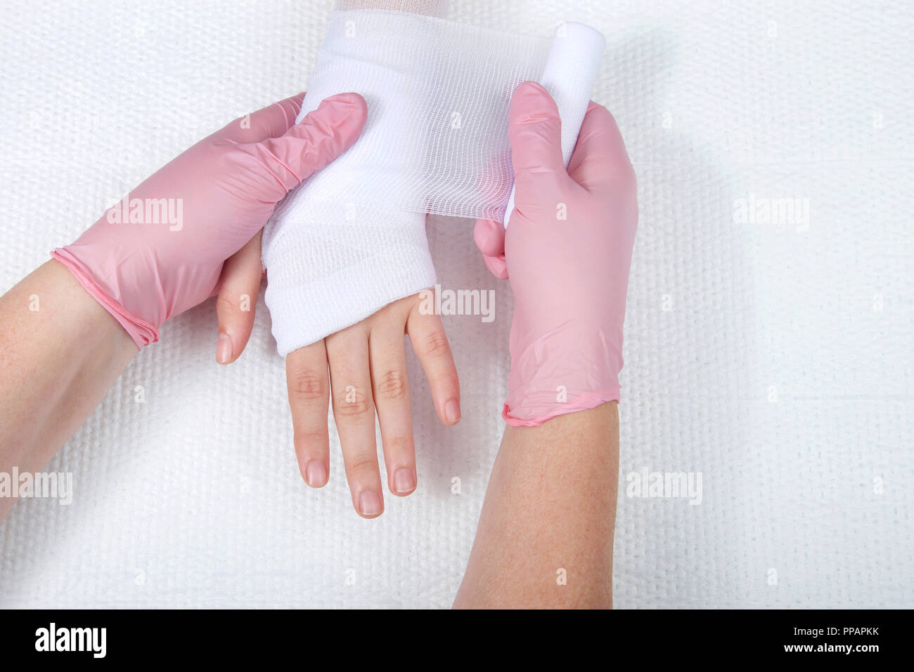 Young female hands wearing pink gloves wrapping gauze on young hand and ...